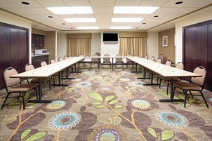 Uma sala de conferências com uma mesa comprida, cadeiras, uma TV de tela plana e um micro-ondas no canto.