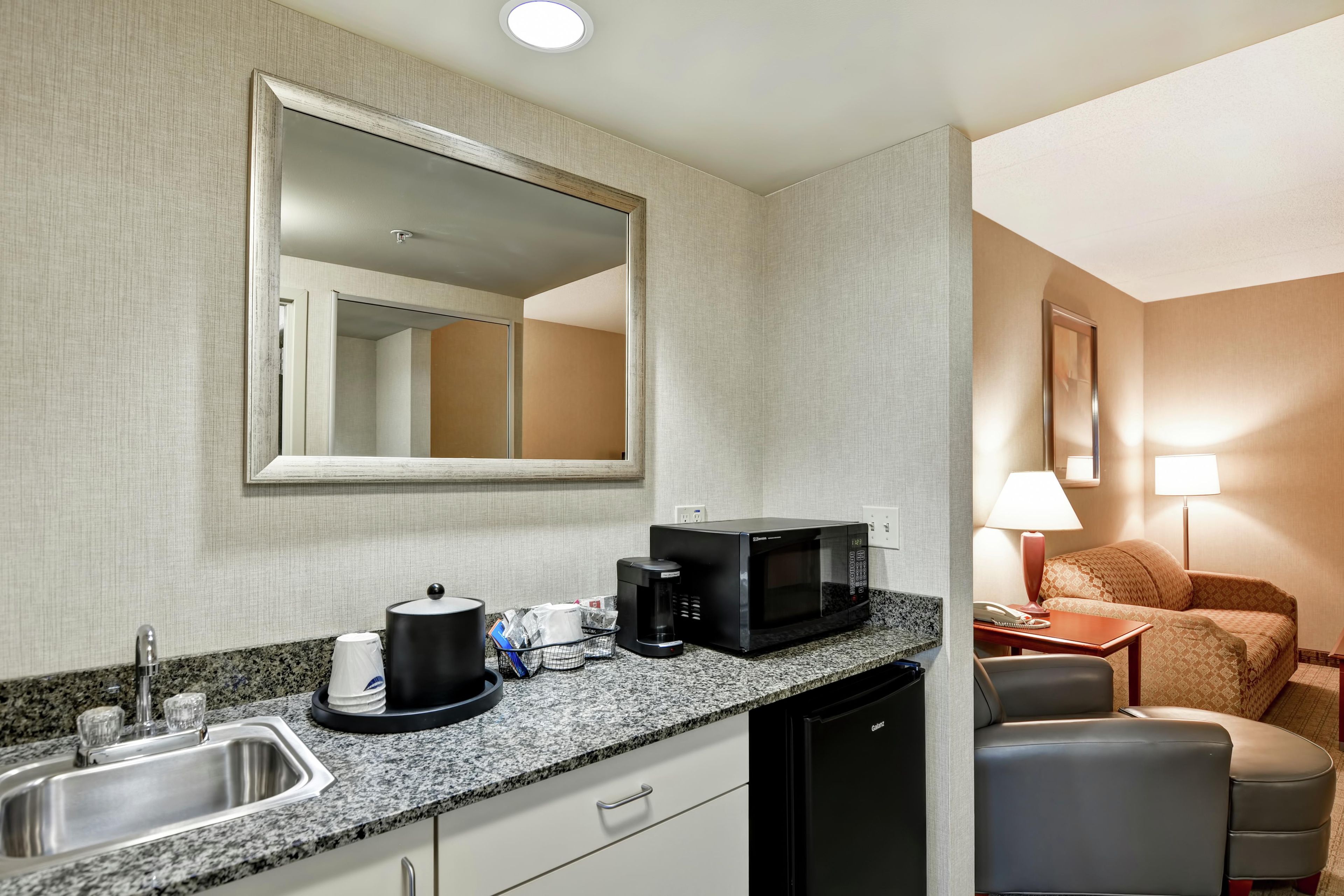 Quarto de hotel compacto com cozinha compacta, cama, escrivaninha e luminária.