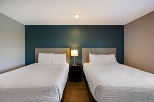 Quarto de hotel com duas camas, uma mesa de cabeceira com abajur e uma luminária no teto.