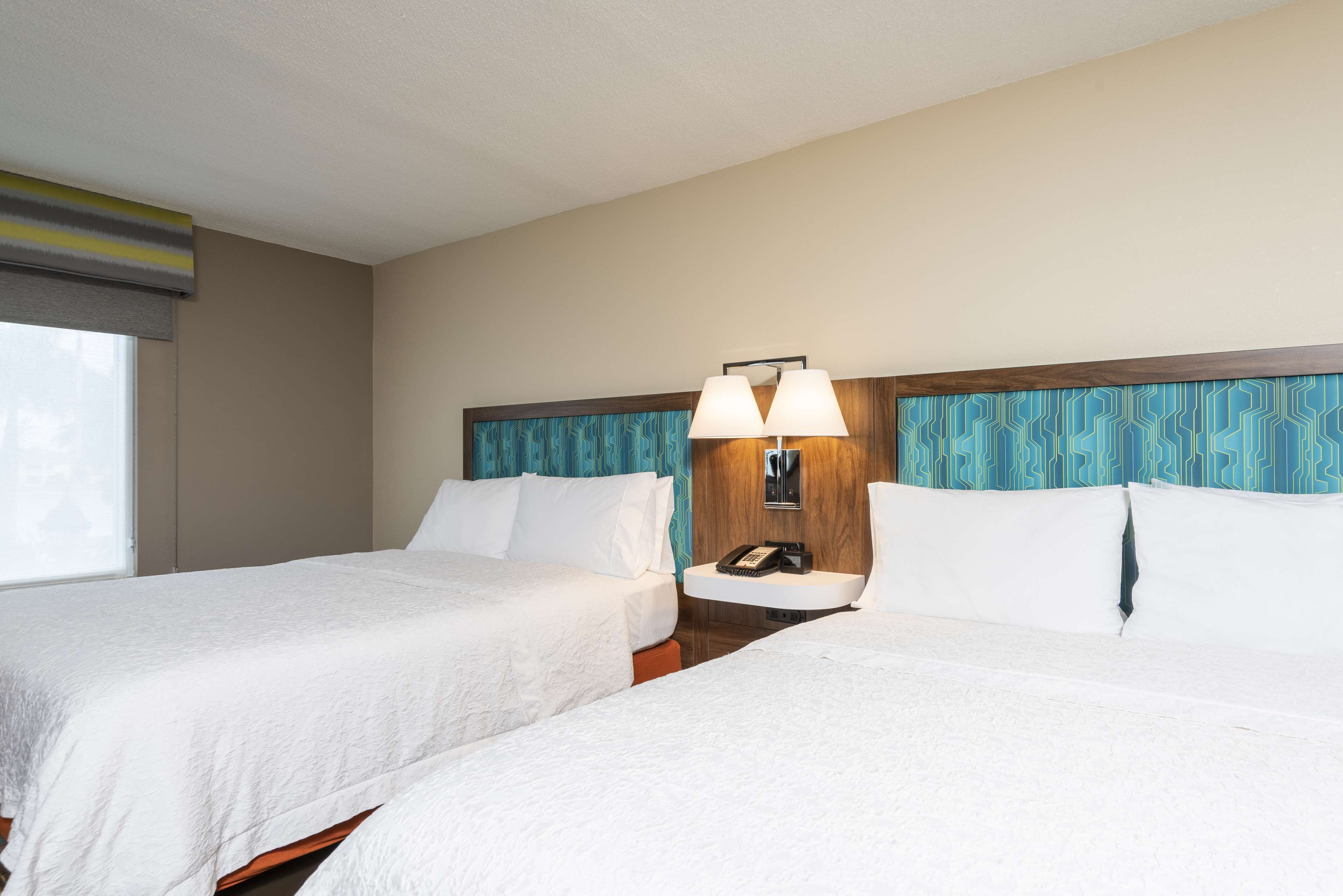 Quarto de hotel com duas camas, uma mesa de cabeceira com abajur e um telefone.