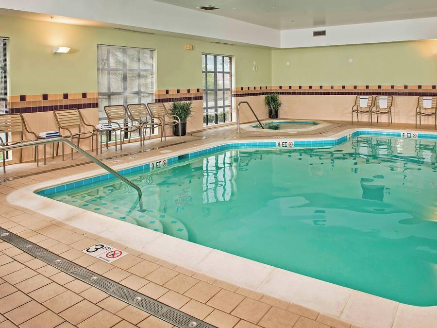 Uma piscina interna com água cristalina, piso ladrilhado e algumas cadeiras de descanso.