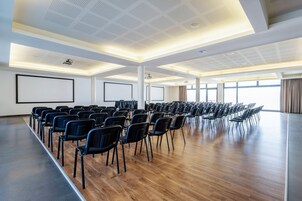 Uma sala de conferência com fileiras de cadeiras, um projetor e uma tela grande.