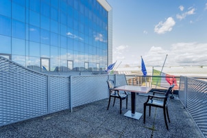 Terraço no telhado com um edifício de vidro, área de estar ao ar livre e bandeiras.