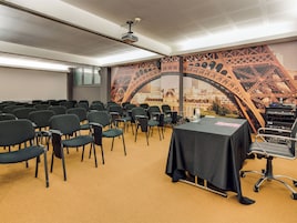 Uma sala de conferências com fileiras de cadeiras, um projetor e uma mesa coberta por um tecido preto.