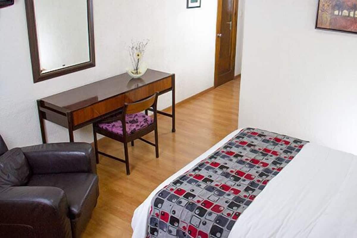 Quarto com cama, escrivaninha, cadeira e porta.