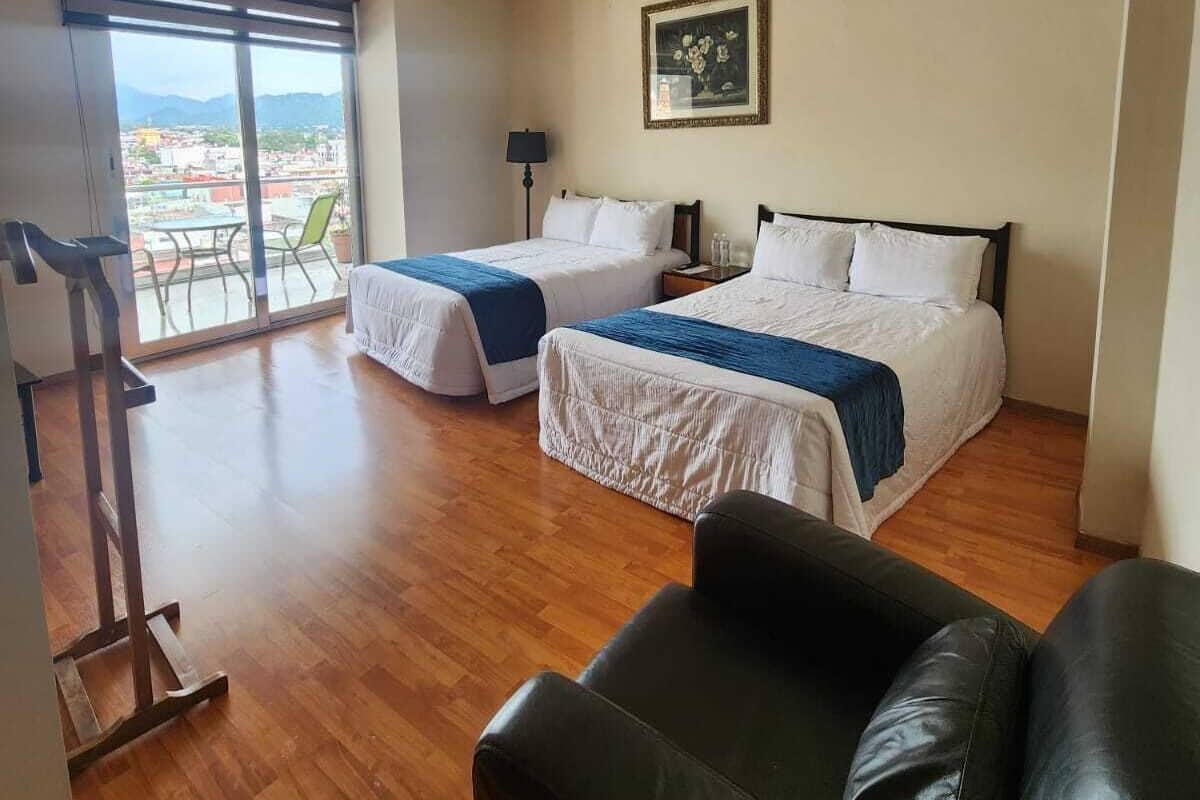 Quarto de hotel com duas camas, esteira, varanda com vista e uma pintura na parede.