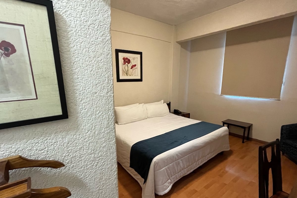 Um quarto com uma cama, uma cadeira, uma mesa pequena e uma janela com persianas.