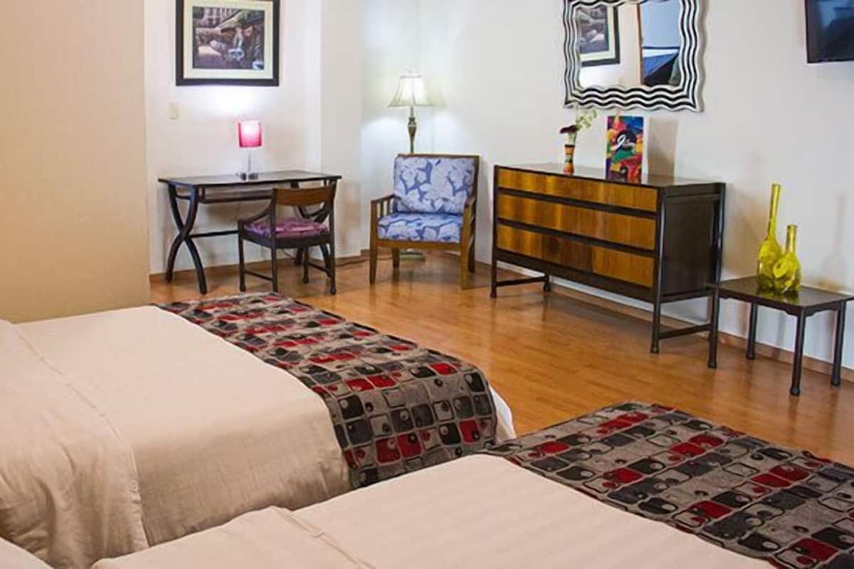 Quarto de hotel com duas camas, uma escrivaninha, uma cadeira, um aparador e uma televisão.