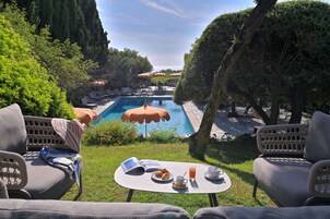 Uma área na beira da piscina com espreguiçadeiras, uma mesa com comida e bebidas, e vista para a piscina.