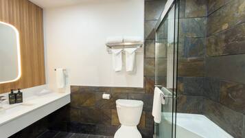 Casa de banho moderna com chuveiro em cabine de vidro, sanita branca e toucador com artigos de higiene pessoal.