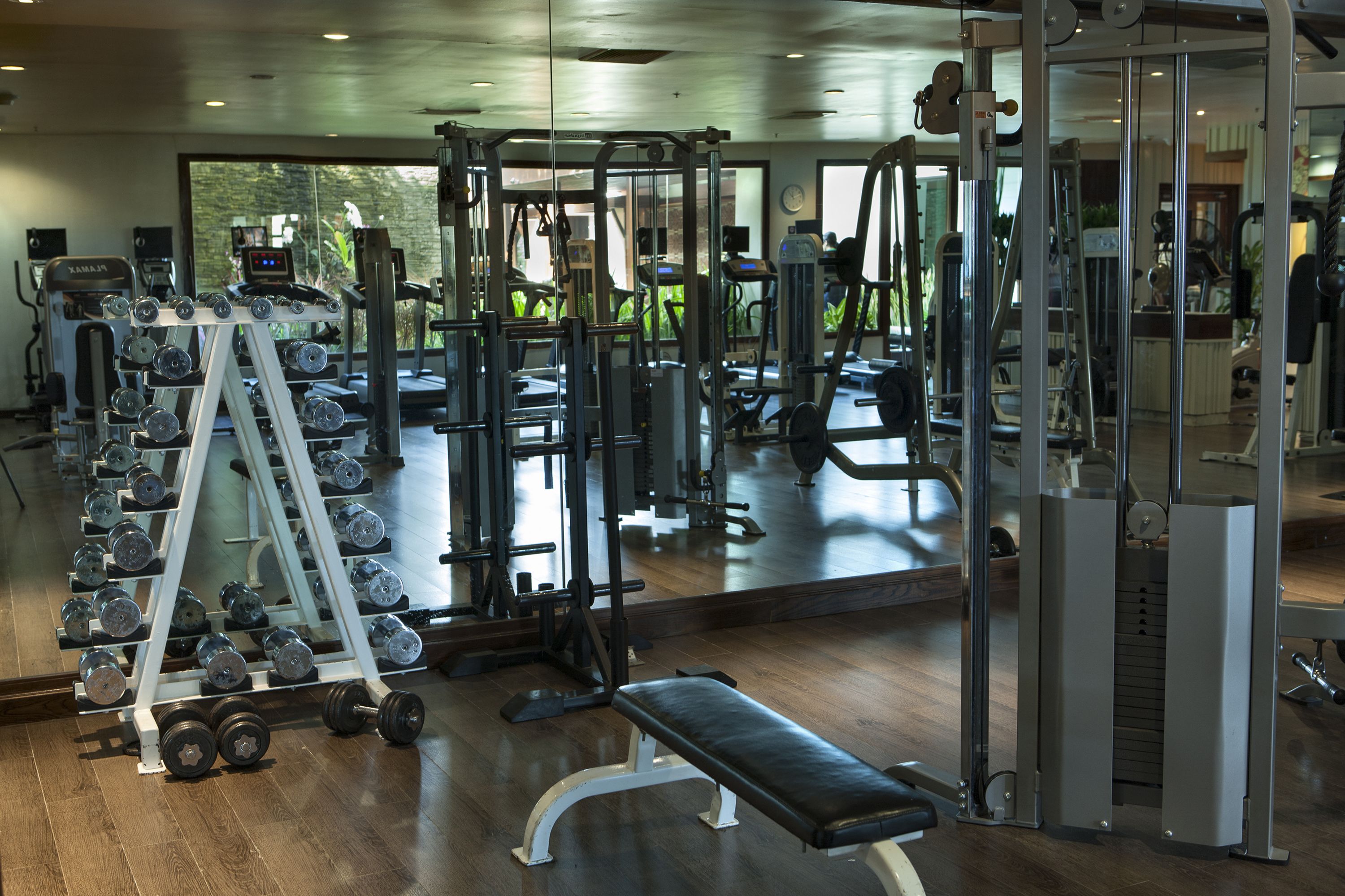 Uma academia com diversos equipamentos de exercício, um banco e um espelho refletindo o espaço.
