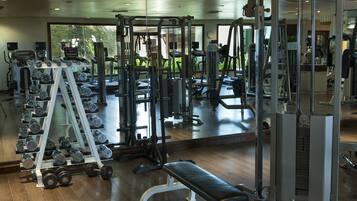 Uma academia com diversos equipamentos de exercício, um banco e um espelho refletindo o espaço.