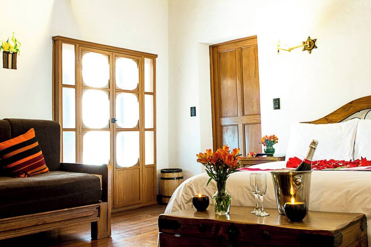 Quarto com cama de madeira, cômoda de madeira, um vaso com flores, uma garrafa de champanhe e uma vela na cômoda.