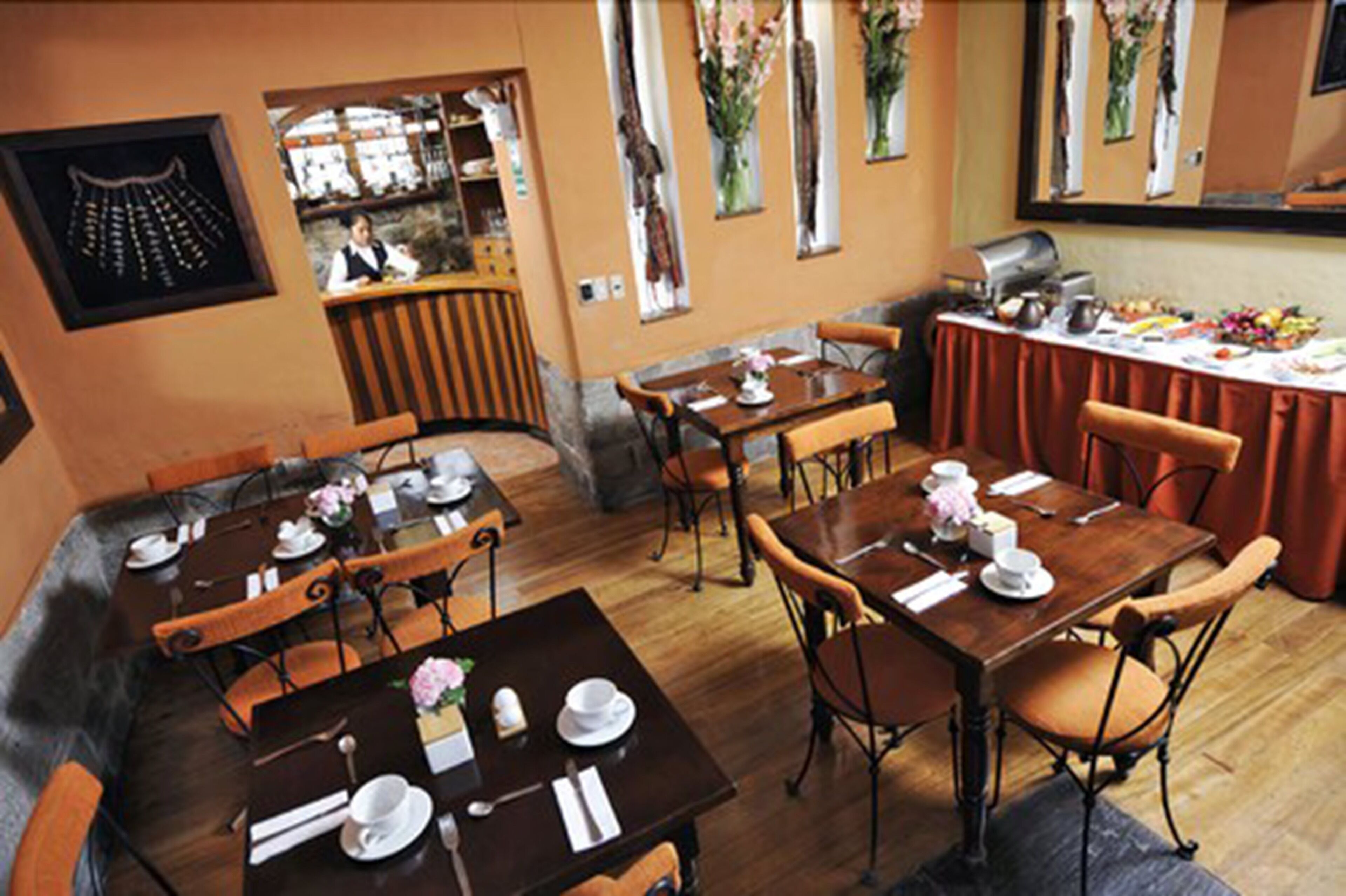 Um restaurante com mesas e cadeiras de madeira, um espaço de bar e um balcão com uma pessoa atrás.