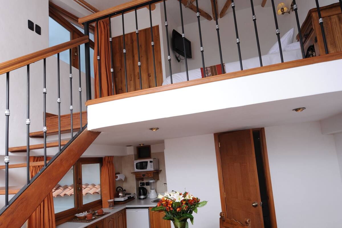 Uma área de refeições de madeira com mesa e cadeiras, uma escada de madeira e uma cozinha com eletrodomésticos.