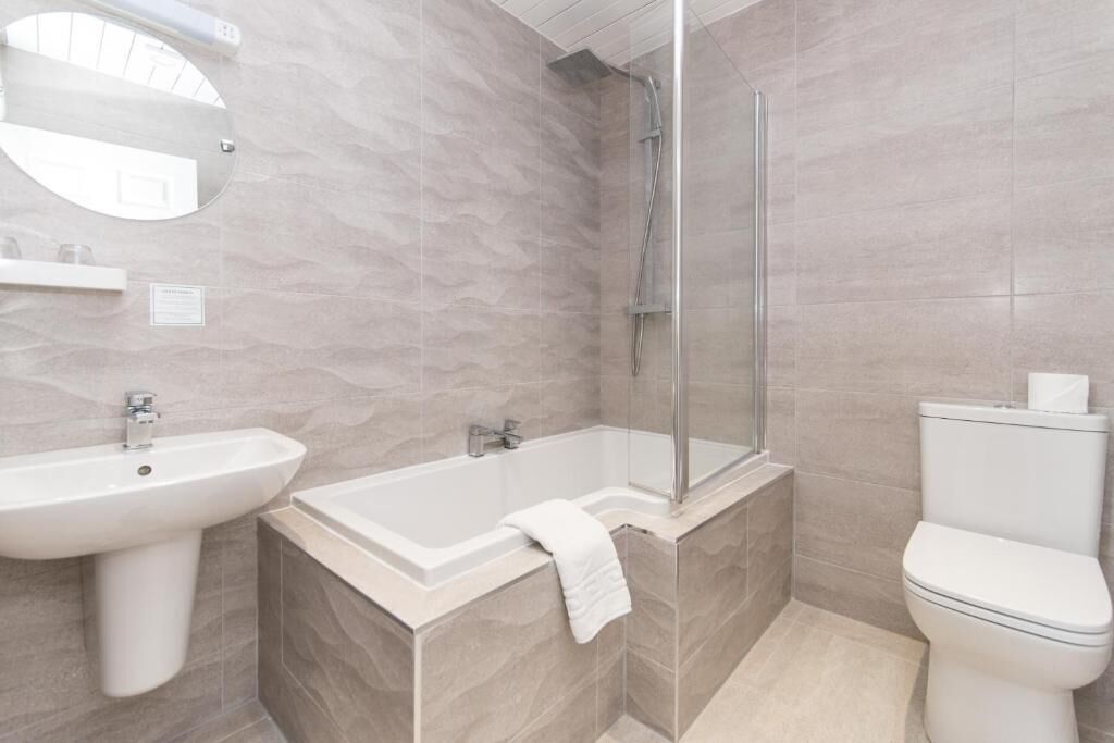 Um banheiro moderno com pia de pedestal, banheira independente, chuveiro com box de vidro e vaso sanitário.