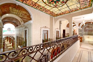 Interior imponente com tetos abobadados, corrimão decorativo e vista para um edifício exterior.