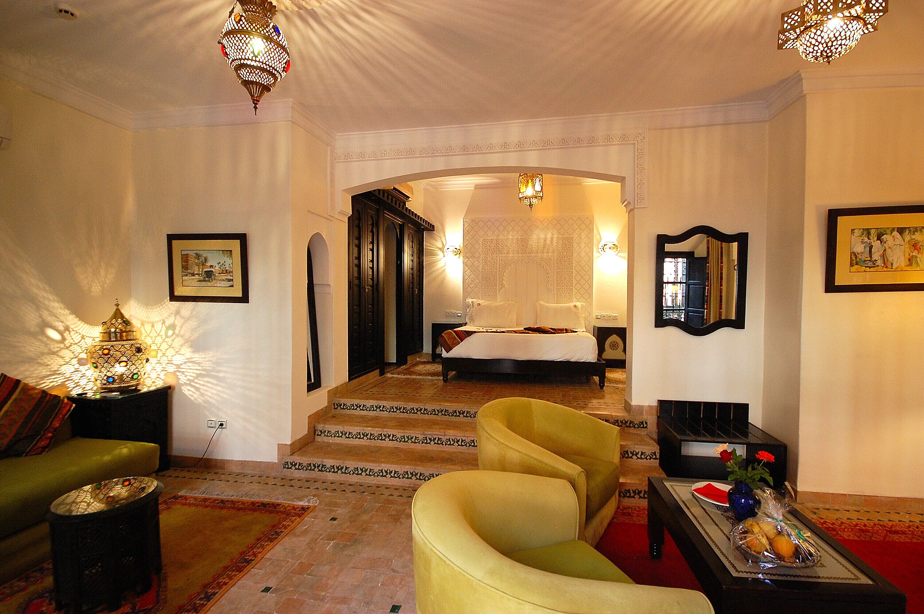 Quarto de hotel com cama, sofá, mesa de centro e uma luminária decorativa.