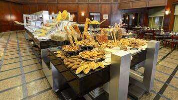 Buffet com diversos alimentos e área de refeições com mesas e cadeiras.