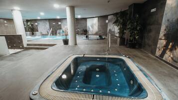 Uma área interna de piscina moderna com uma banheira de hidromassagem central, rodeada por pilares de pedra e plantas em vasos.