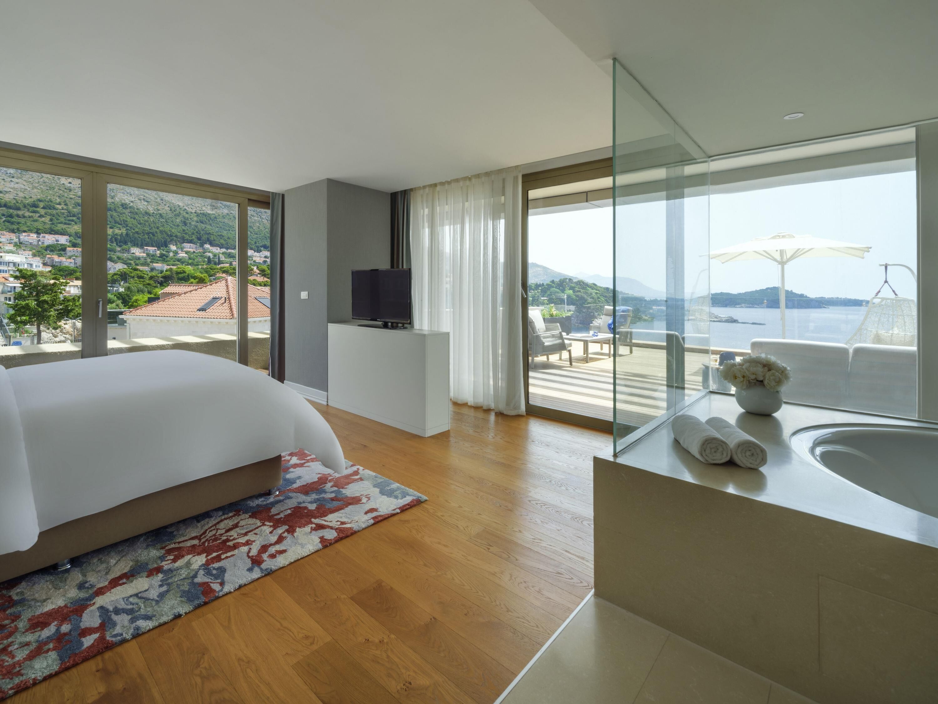 Quarto de hotel moderno com uma cama grande, televisão, varanda com vista para o mar e banheiro com banheira.