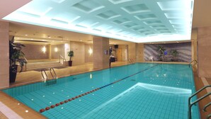 Uma piscina interior com chão em mosaico, teto com iluminação embutida e área de estar com degraus que levam a uma porta.