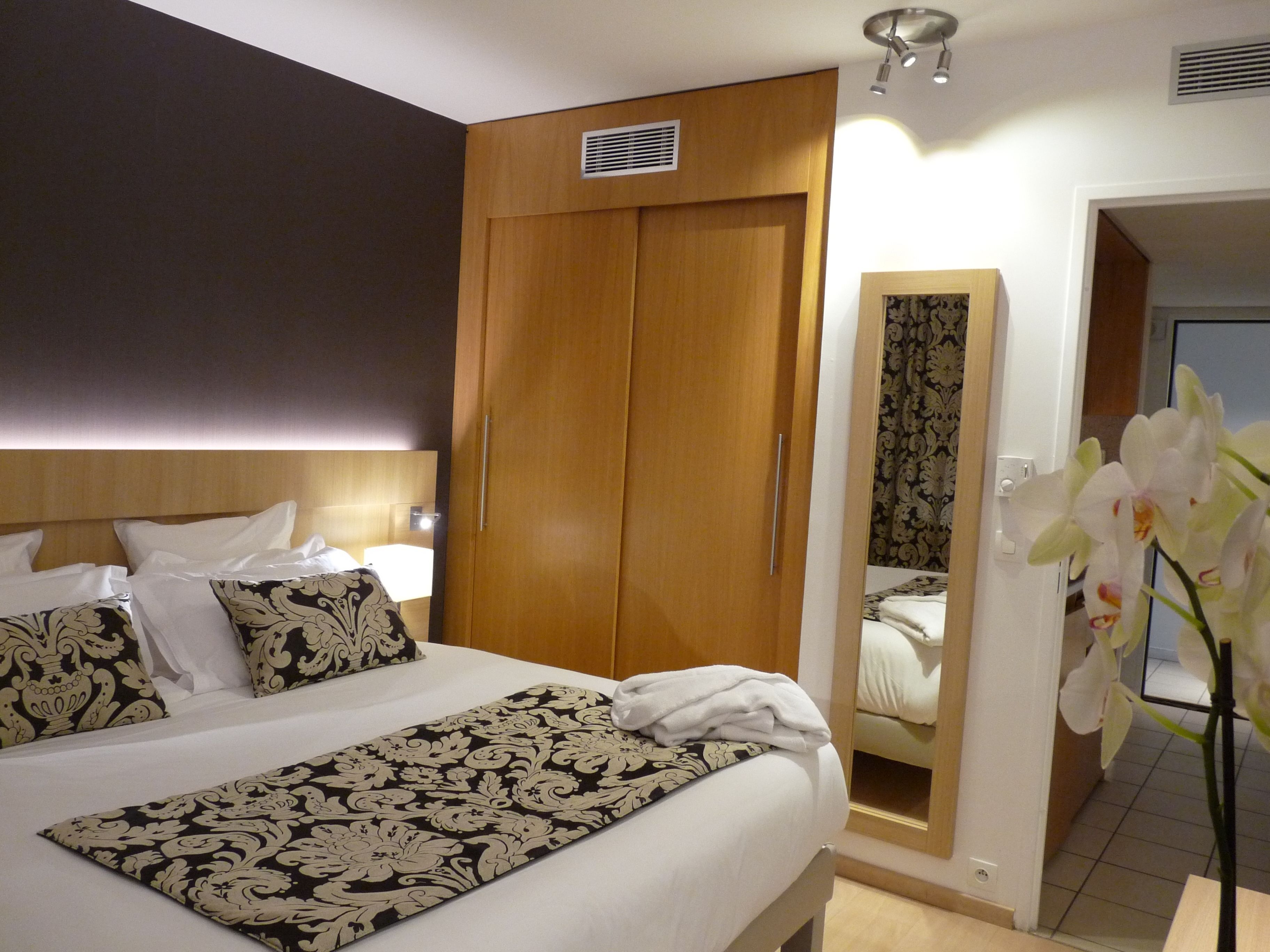 Quarto de hotel com uma cama grande, um guarda-roupa, um espelho e uma orquídea em vaso.