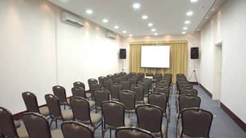 Uma sala de conferências com fileiras de cadeiras, uma tela de projeção e alto-falantes.