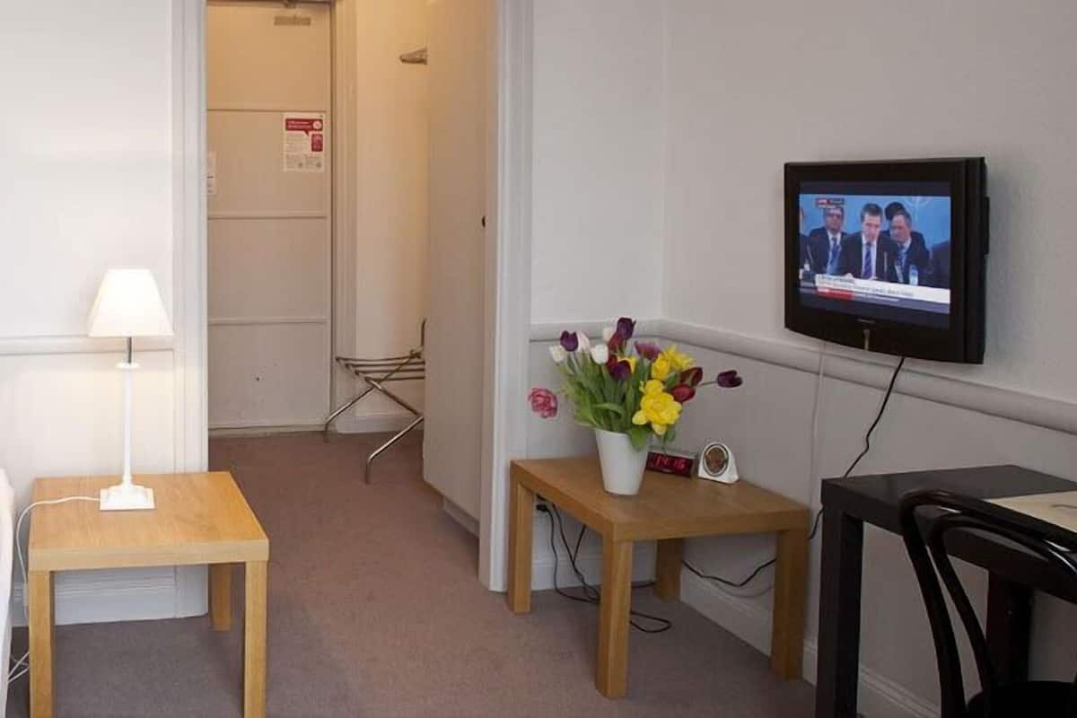 Quarto de hotel com cama, escrivaninha, cadeira, televisão e uma pequena mesa com um vaso de flores.
