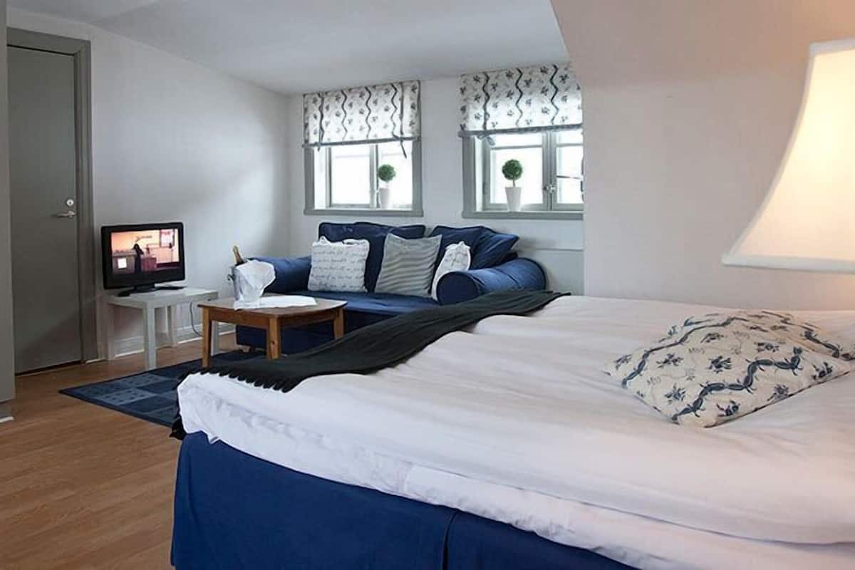 Quarto com cama, escrivaninha, televisão e janela com cortinas.