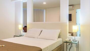 Quarto de hotel com cama, abajures, telefone e espelho.