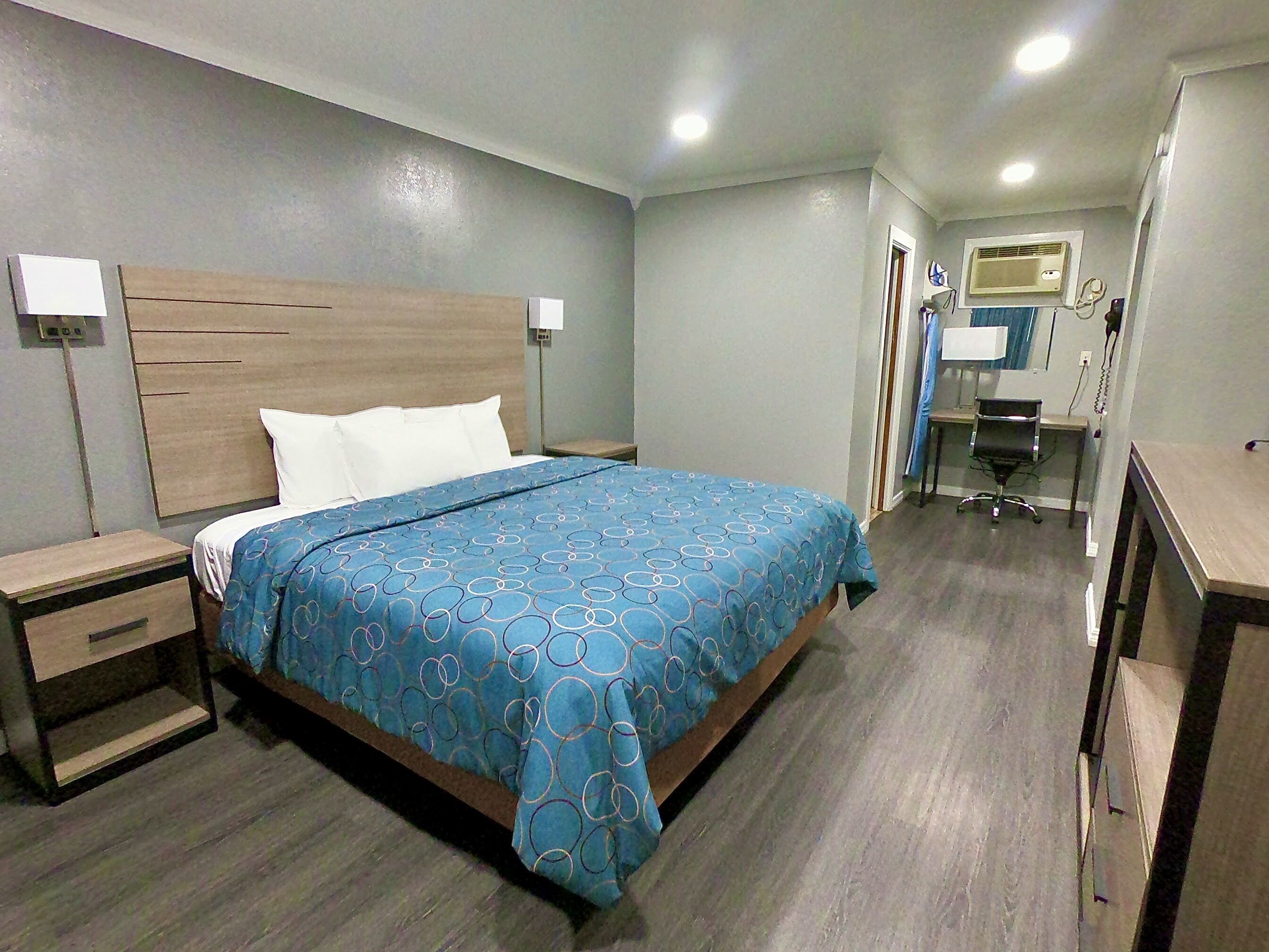 Quarto com cama, mesas de cabeceira, escrivaninha e aparelho de ar condicionado.