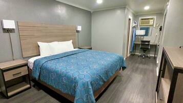 Quarto com cama, mesas de cabeceira, escrivaninha e aparelho de ar condicionado.
