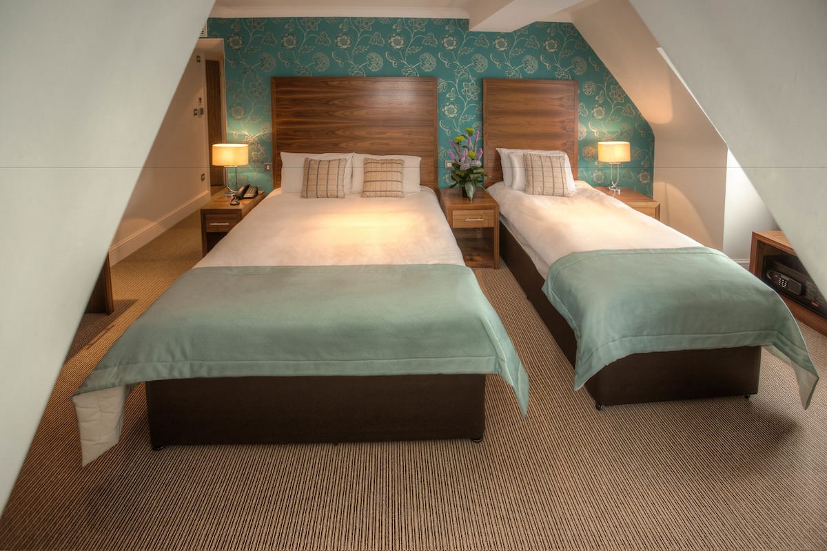 Quarto de hotel com duas camas, cabeceiras de madeira e um padrão floral no papel de parede.