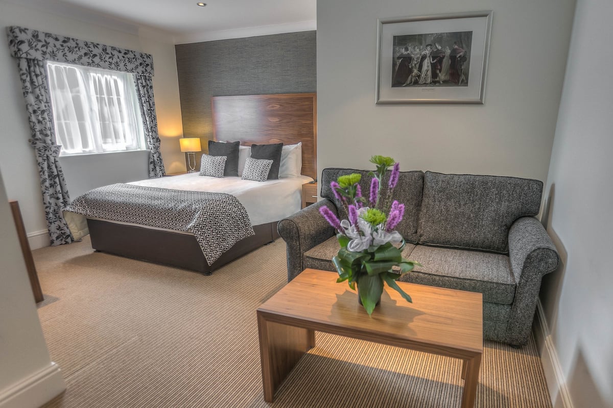 Quarto de hotel com cama, sofá, mesa de centro e um quadro na parede.