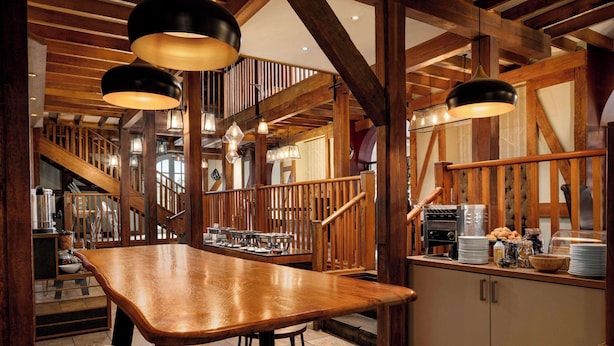 Uma área de jantar de madeira com uma mesa grande e cadeiras, uma escada e uma cozinha com diversos eletrodomésticos e utensílios.