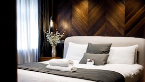 Uma cama bem arrumada com roupa de cama branca e cinza, um vaso com flores e uma parede de madeira com padrão em chevron.