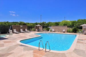 Piscina retangular com borda curva, cercada por um muro de tijolos e uma grade de metal.