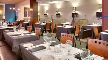 Um restaurante com várias mesas preparadas para refeições, cada uma com pratos, talheres e copos.