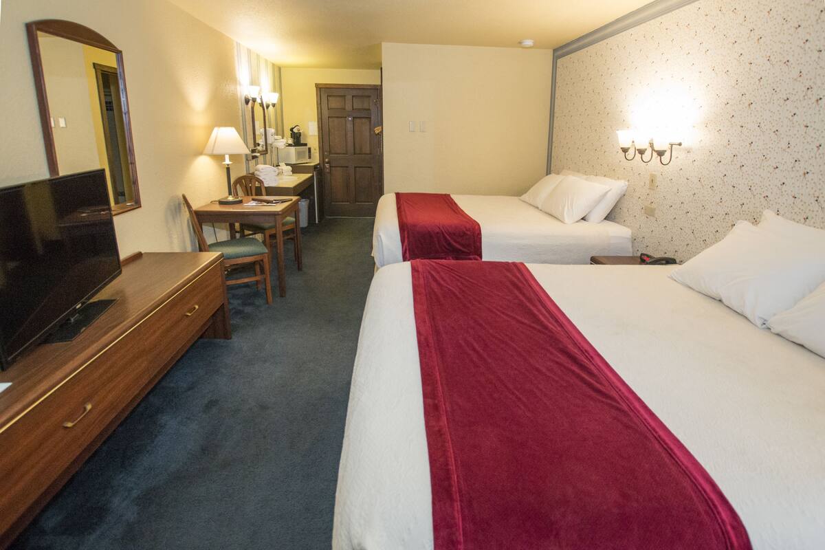 Quarto de hotel com duas camas, uma escrivaninha, uma cadeira, uma televisão e uma porta que dá para um banheiro.