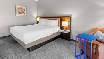 Quarto de hotel com uma cama grande, mesa de cabeceira com abajur, uma mesinha e um sofá.