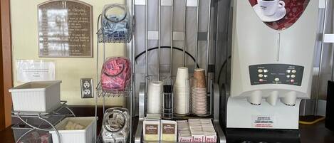 Uma estação de café com máquina Nescafe, copos descartáveis e variedade de cápsulas de café.