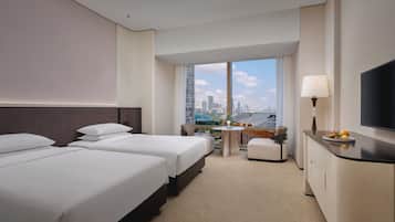 Quarto de hotel com duas camas, uma escrivaninha, uma televisão e vista para a paisagem urbana.