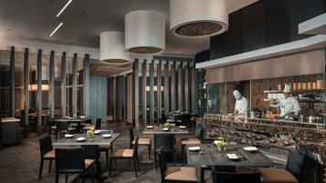 Um restaurante moderno com pé-direito alto, iluminação pendente e uma área de cozinha central.