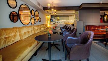 Uma área de estar moderna com um sofá dourado aconchegante, poltronas de couro e uma mesa redonda central com um vaso de flores.