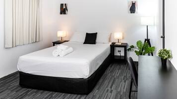 Quarto de hotel com cama, mesas de cabeceira, luminárias, escrivaninha e um vaso de plantas.