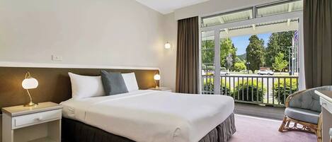 Quarto de hotel com uma cama grande, uma escrivaninha, uma cadeira e varanda com vista para a rua.