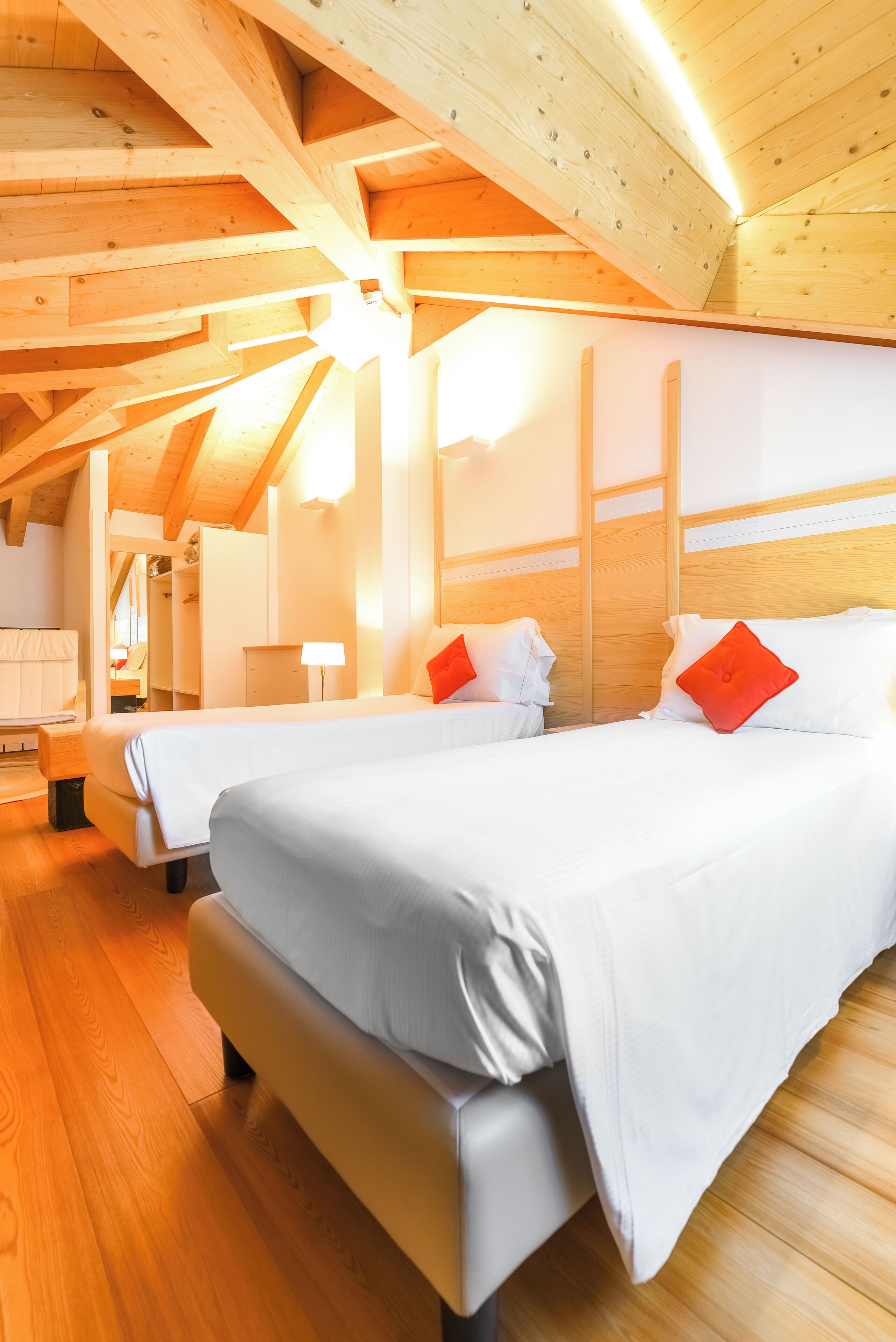 Quarto com duas camas, vigas de madeira e piso de madeira.