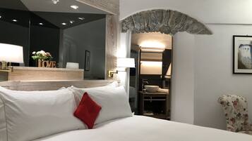 Quarto de hotel com uma cama grande, cabeceira de madeira, um espelho, toucador com pia e uma obra de arte emoldurada na parede.