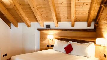 Quarto com teto de madeira, cama com roupa de cama branca, travesseiro vermelho e abajures laterais.